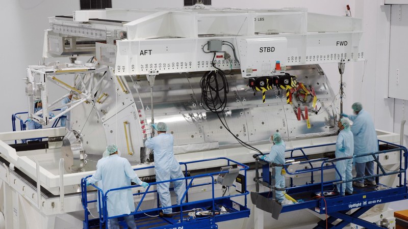 An overhead crane is lowered onto the Columbus module to lift it out of ...